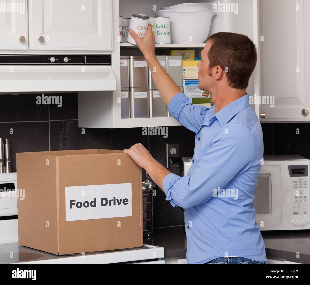 USA, Illinois, Metamora, Man placing canned food in kitchen cupboard ...