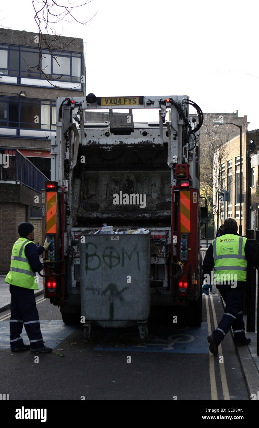 a refuse collector operating a dust cart while collecting rubbish in a ...