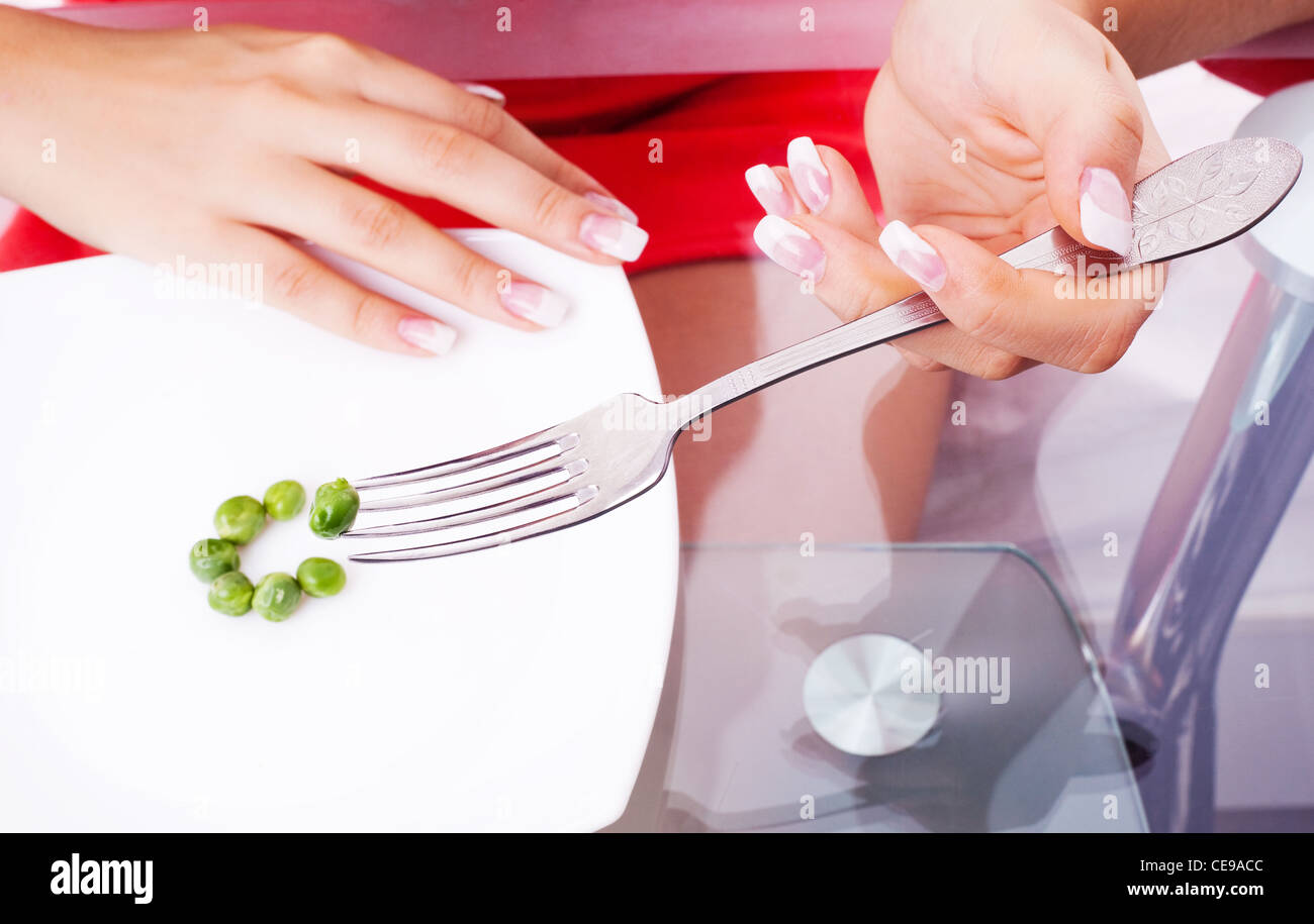 hands of a woman sitting by the table, keeping a diet and eating peas ...