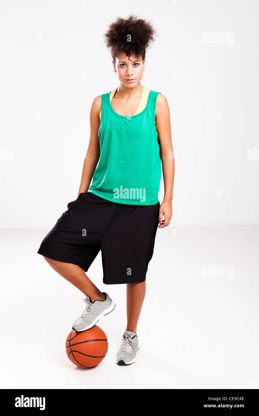 Athletic woman standing with a basketball under her foot. Studio shot ...