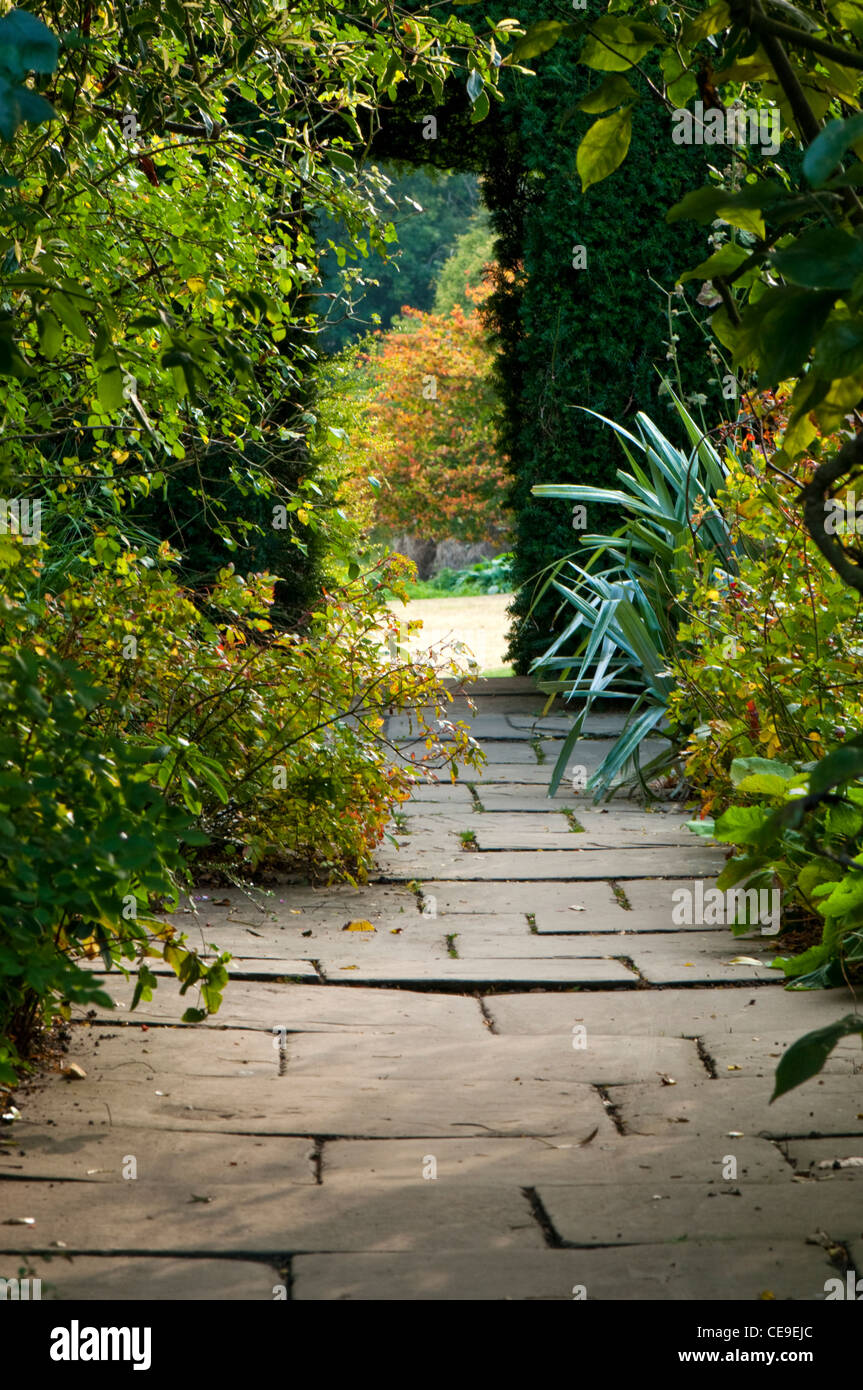 An old stone pathway leading through a lush green garden Stock Photo ...