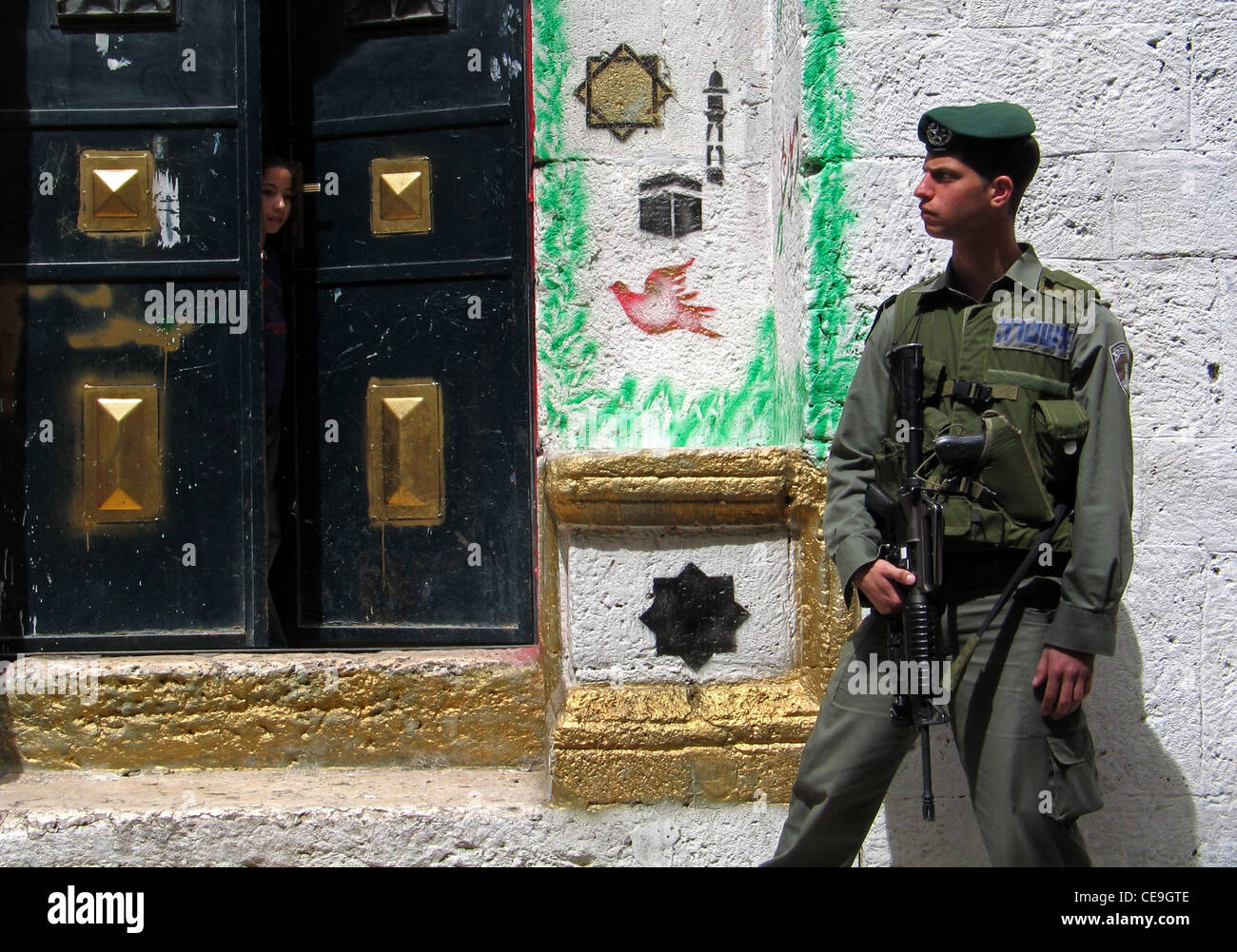 A young Palestinian girl peeps out from a door and looks at an armed ...