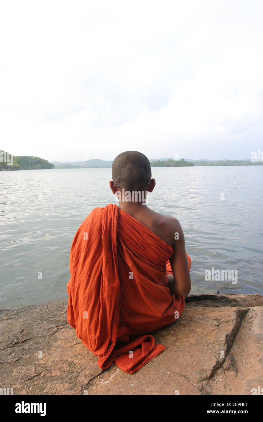 A young monk at a Buddhist temple meditates infront of a large lake ...