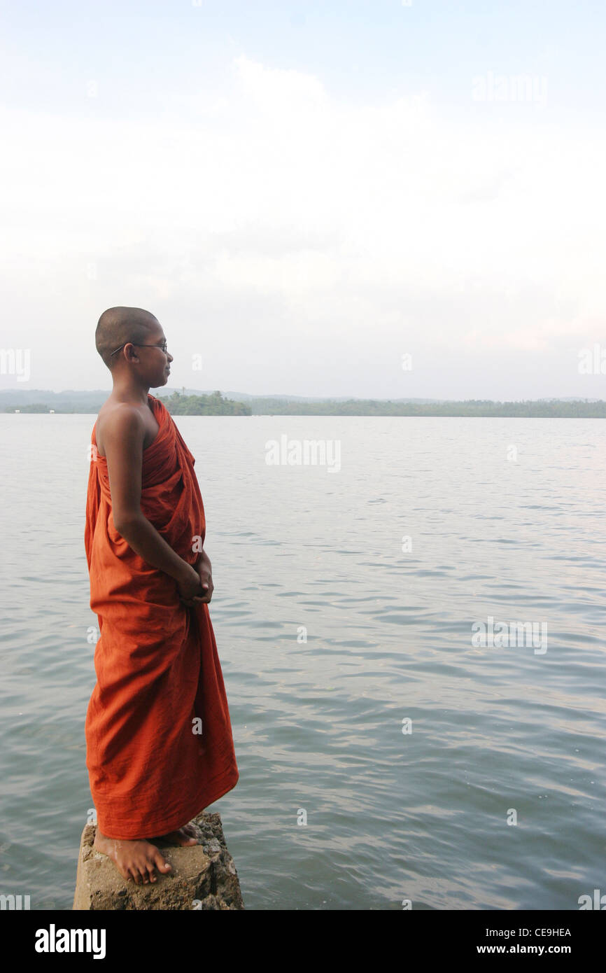 A young Buddhist Monk stands in front of a lake looking out over the ...