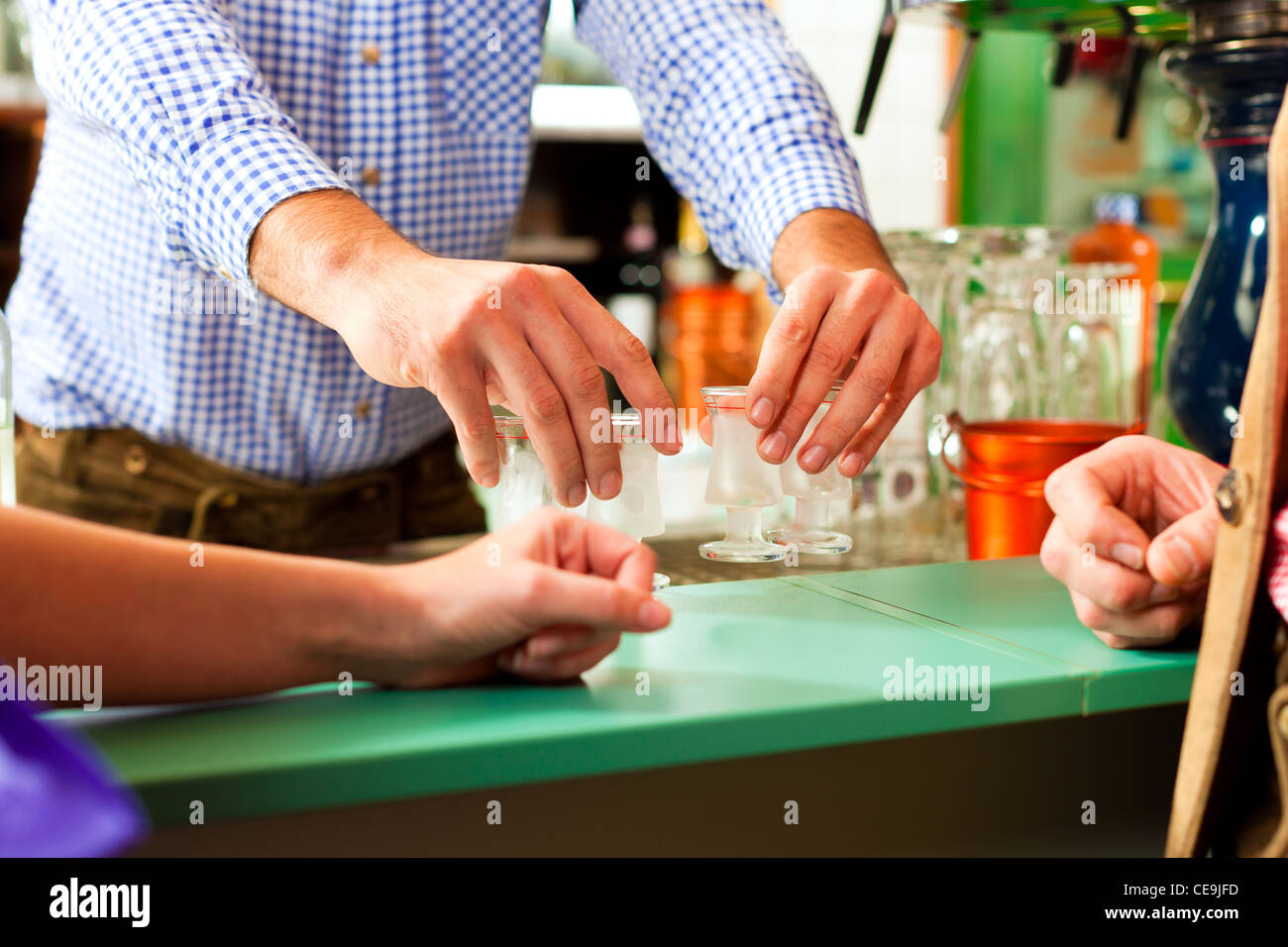 Barkeeper putting hard liquor glasses on bar, people waiting for a ...