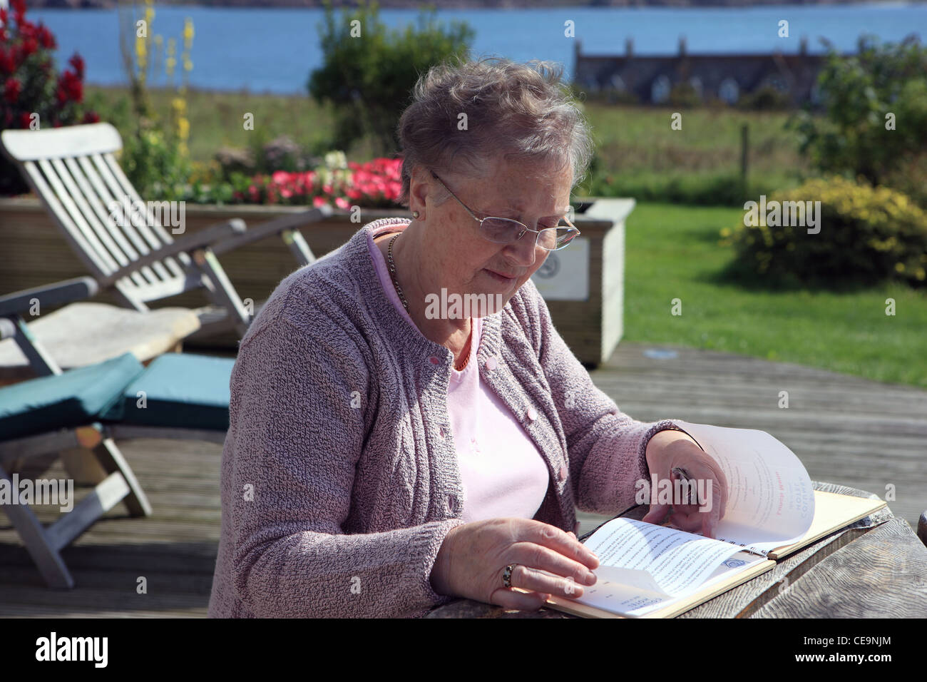 Elderly lady reading a menu in the gardens of a restaurant in summer ...