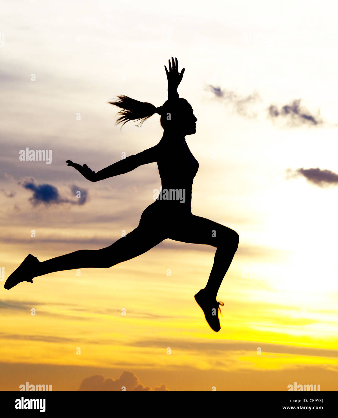 Silhouette of a beautiful jumping woman against yellow sky with clouds ...