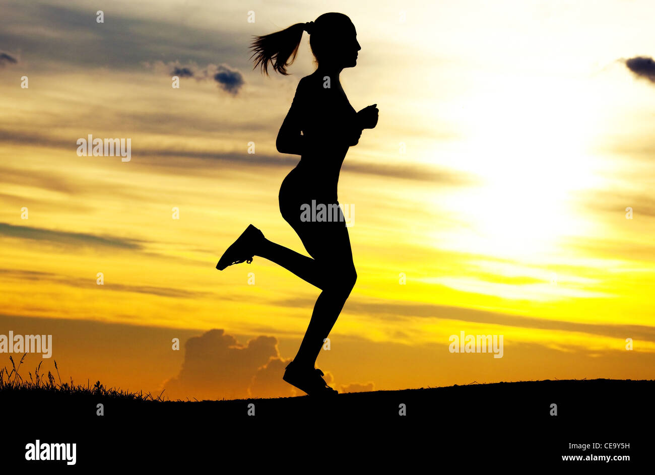 Silhouette of a beautiful running woman against yellow sky with clouds ...