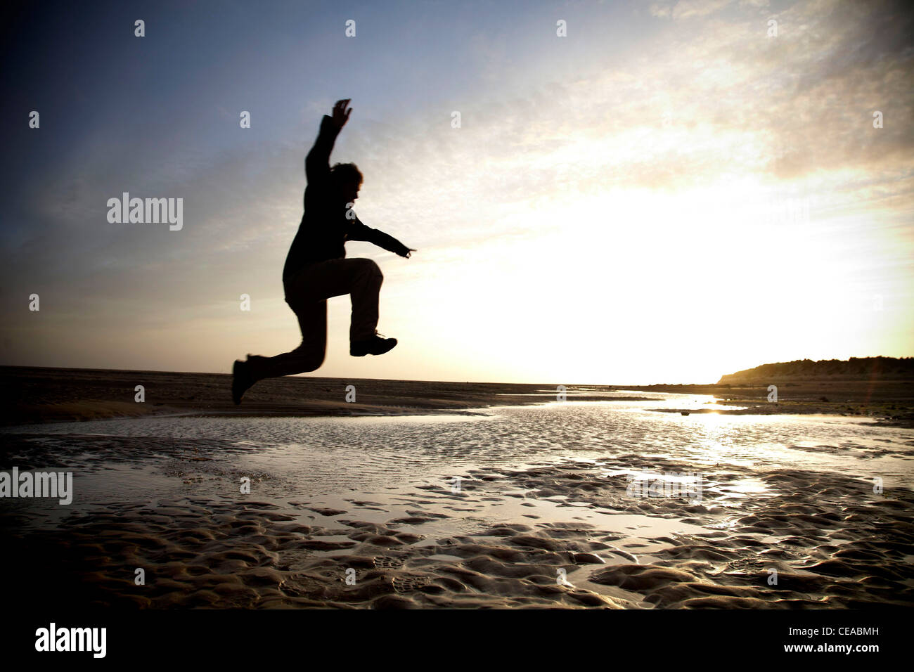 Jumping across water on a beach in Barmouth Stock Photo - Alamy