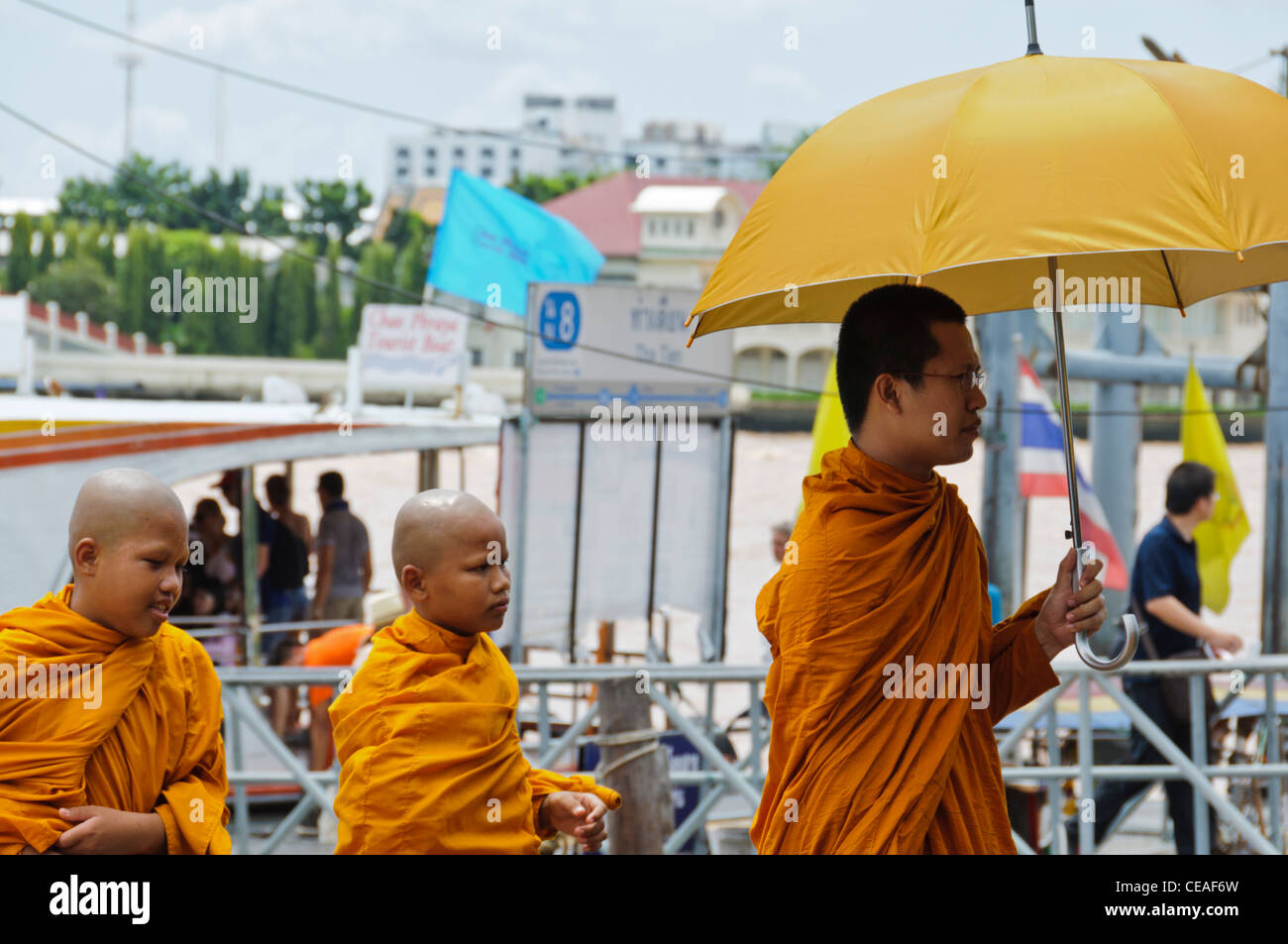 Senior Buddhist Thai Monk with yellow umbrella followed by two novice ...