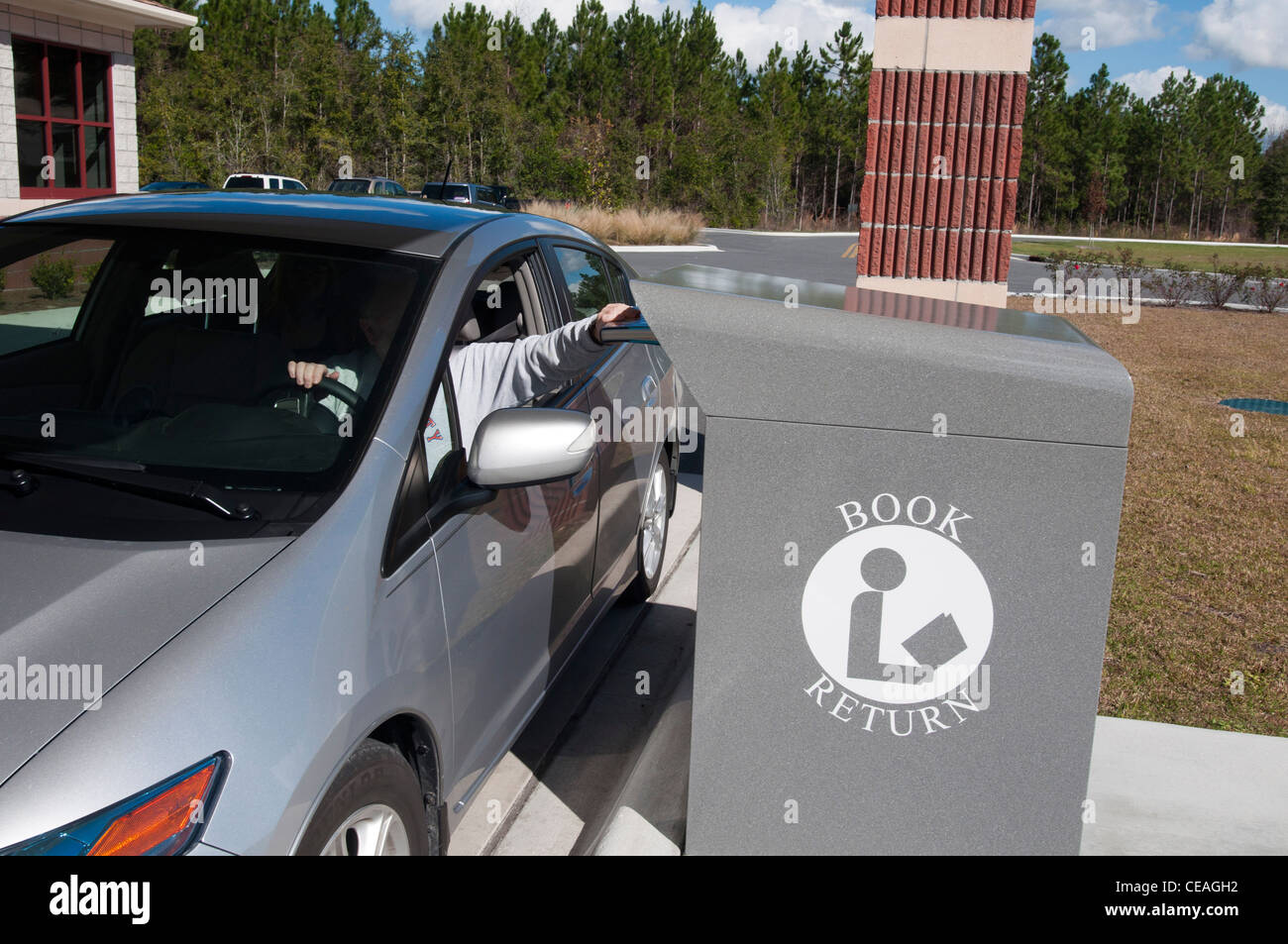 Man in a car dropping a book at drive in library book return box ...