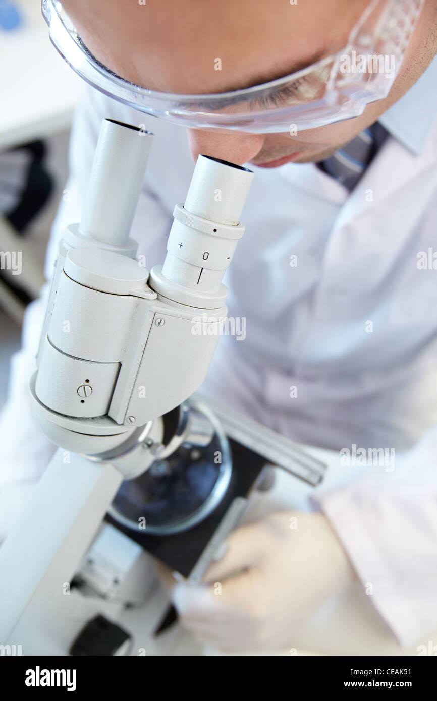 Male scientist in protective eyeglasses looking through the microscope ...