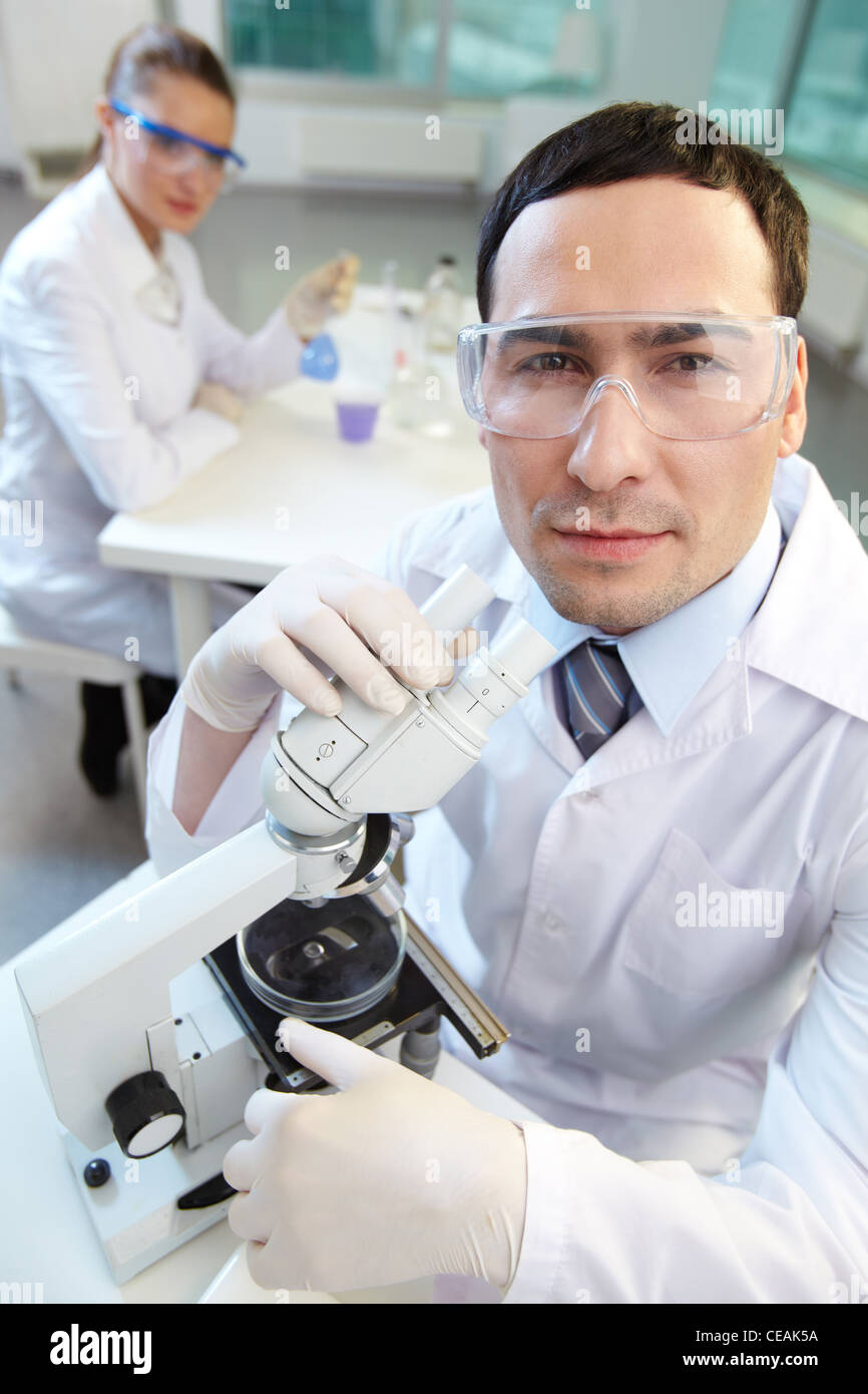Man with a microscope and his colleague looking at camera Stock Photo ...