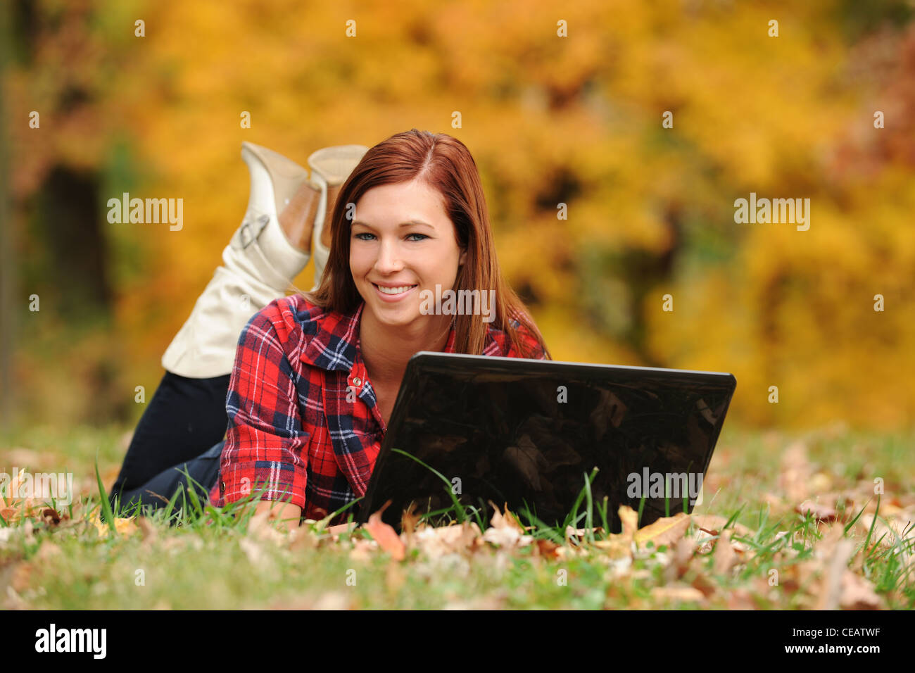 Young Woman laying down with a laptop computer with fall background out ...