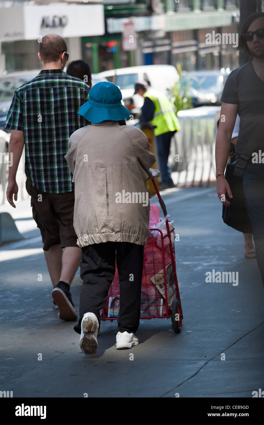 Urban recycling of rubbish by a street person pushing a cart of rubbish ...