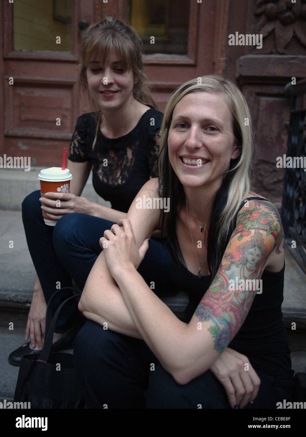 Two young women, one with tattoo, sitting on a stoop, Brooklyn, New ...