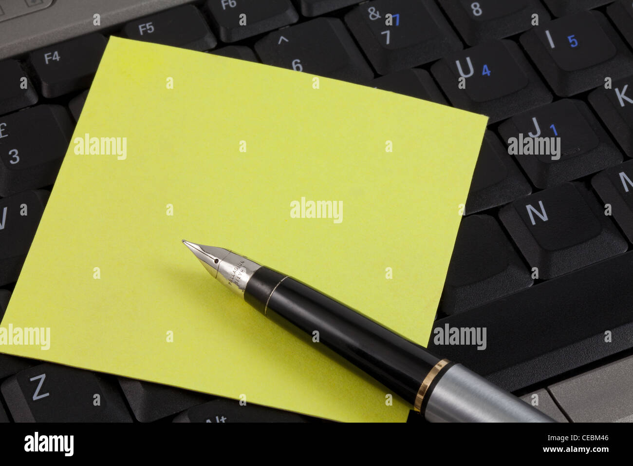 A yellow post it note and a fountain pen on a laptop keyboard. With ...