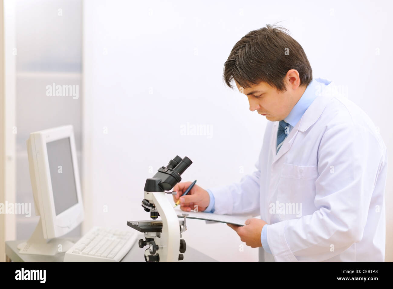 Researcher using microscope in medical laboratory and taking notes ...