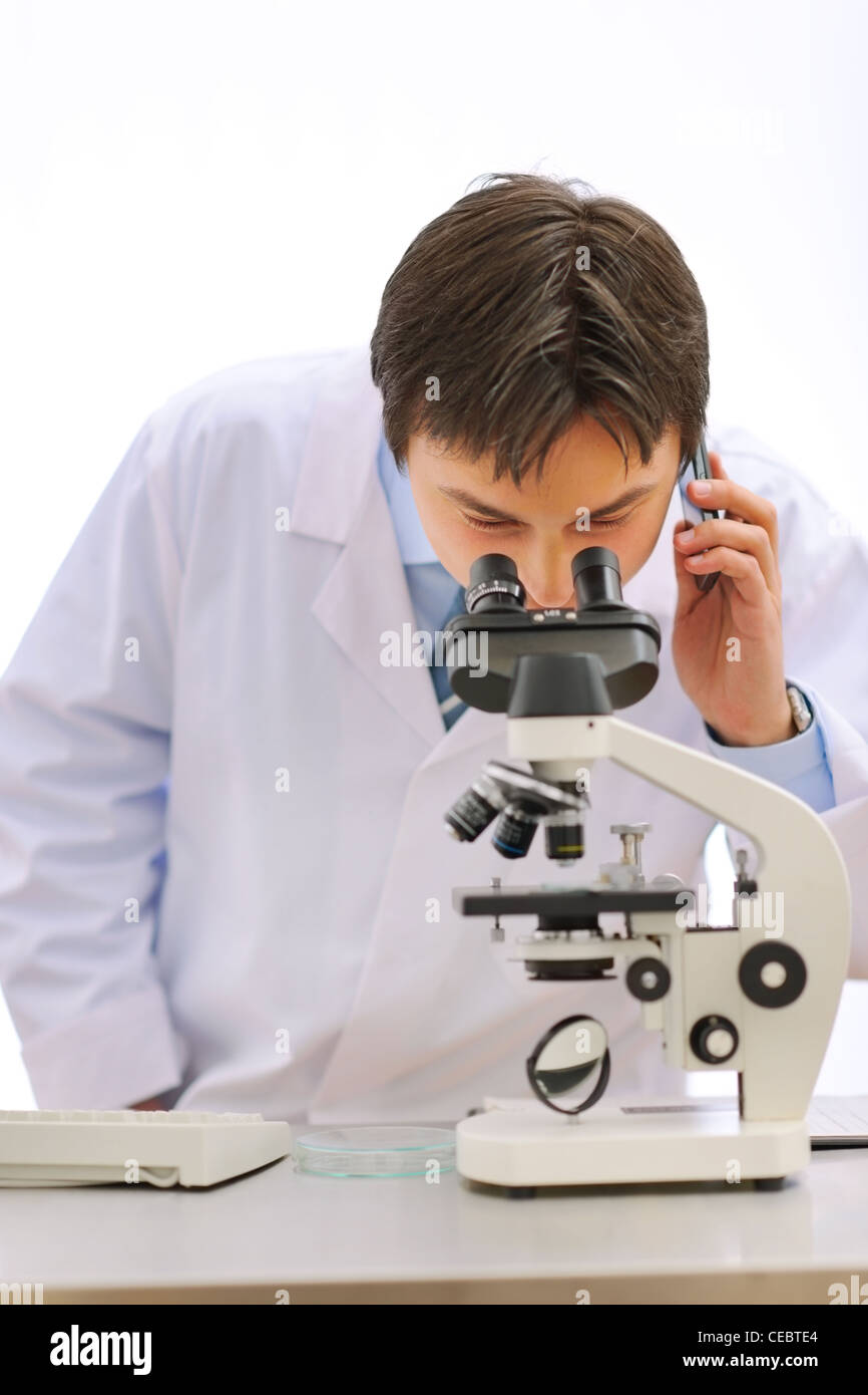 Researcher looking in microscope and speaking mobile in medical ...