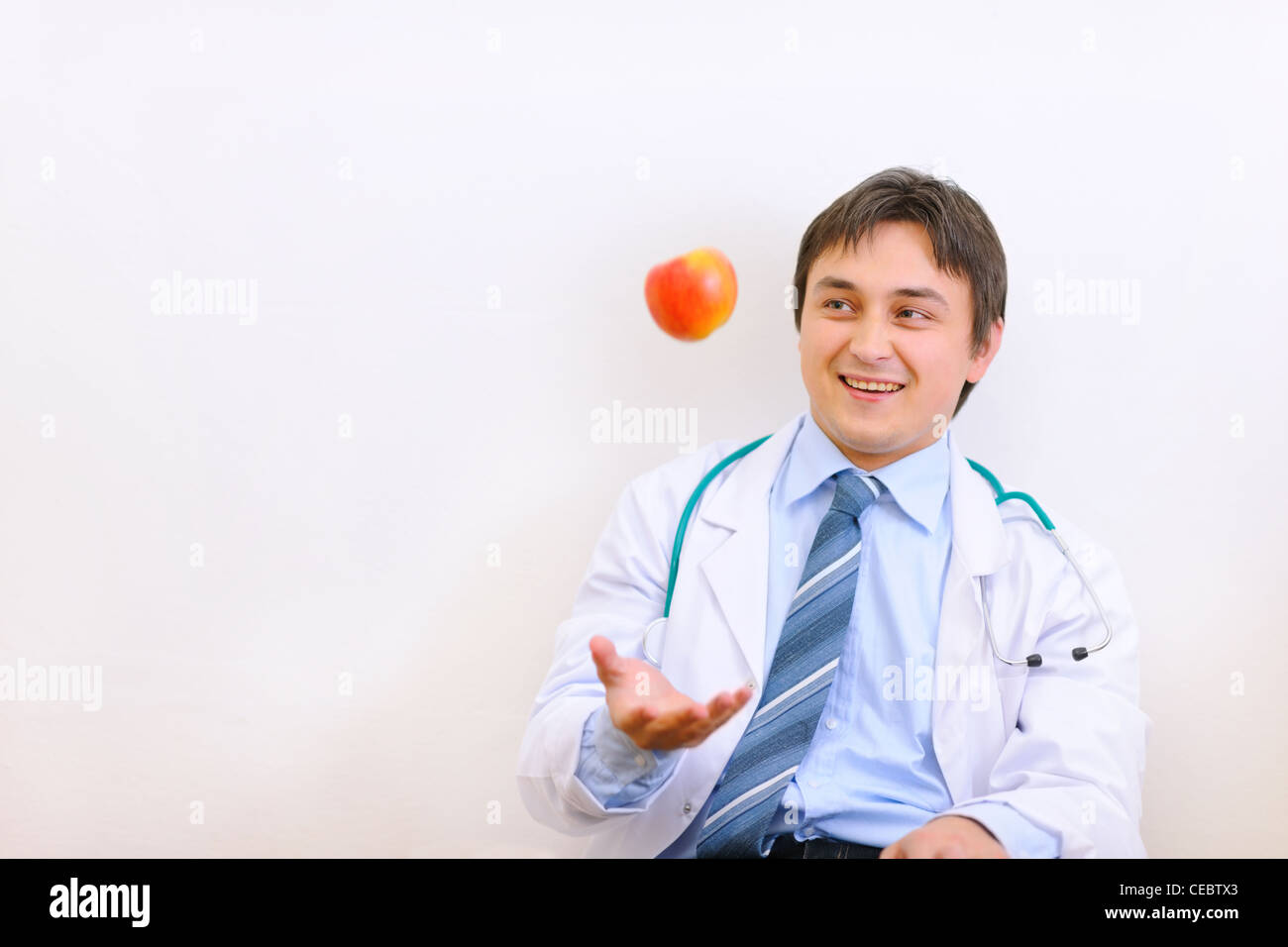 Smiling medical doctor sitting on floor and throwing up apple Stock ...