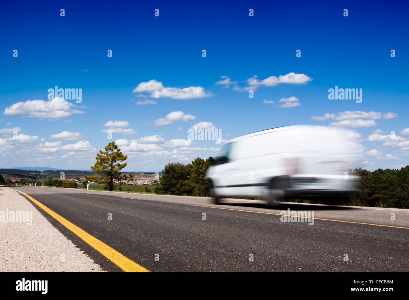 White van in a country road with some trees and a great blue sky above ...