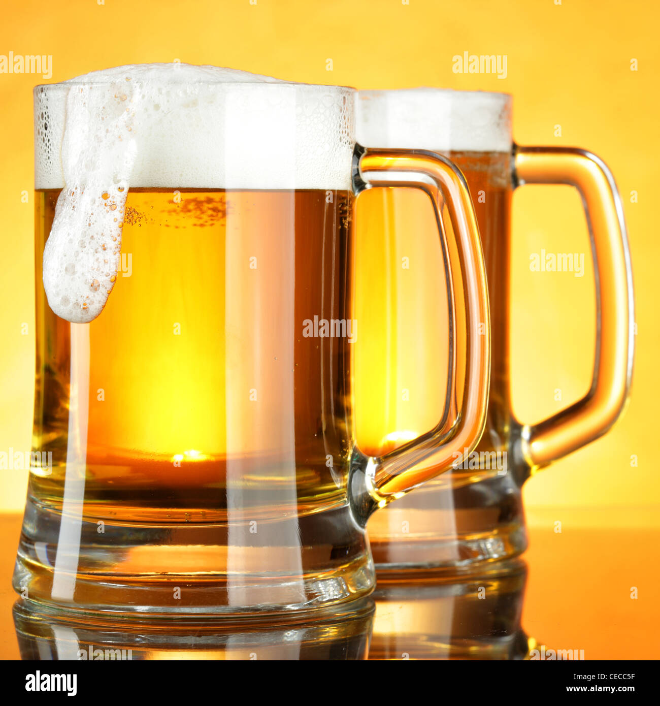 Beer mugs with froth over yellow background Stock Photo - Alamy