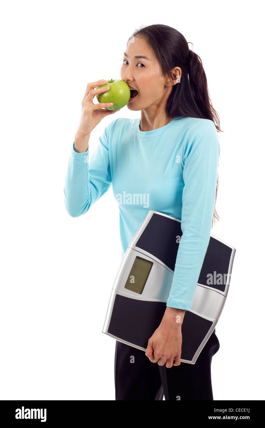 Attractive healthy Asian woman eating a green apple, carrying a weight ...