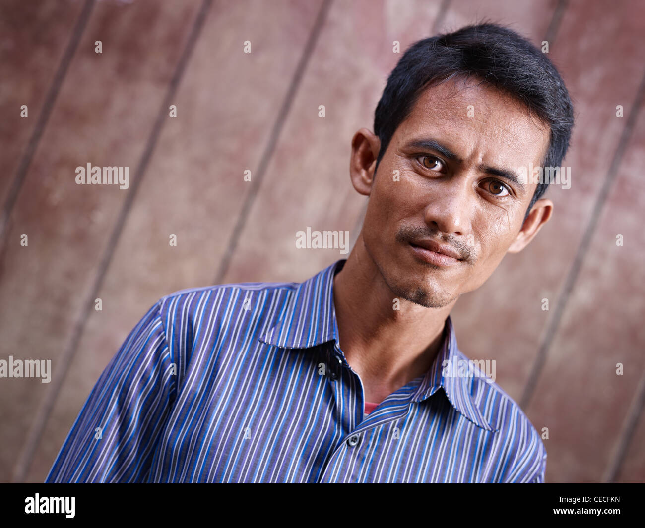 Portrait of mid adult asian man staring at camera against brown wall ...