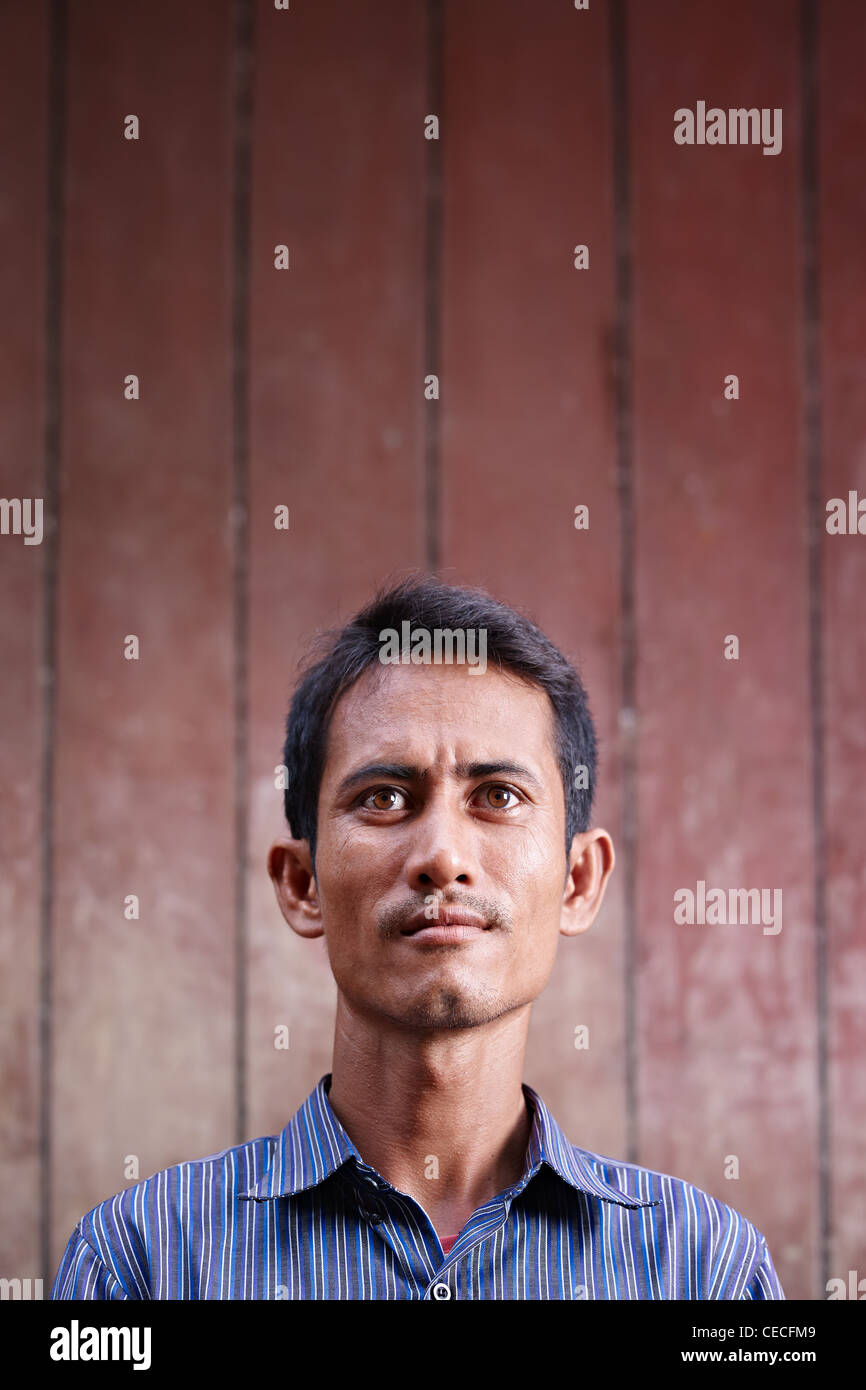 Portrait of mid adult asian man looking up against brown wall. Copy ...