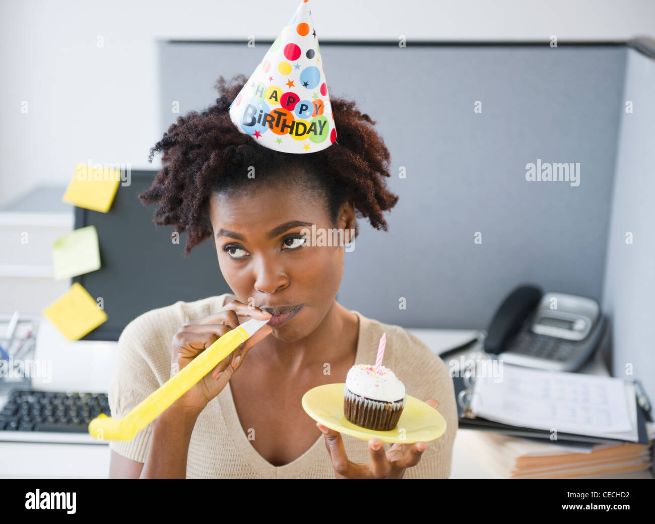Black businesswoman blowing party blower at desk Stock Photo - Alamy