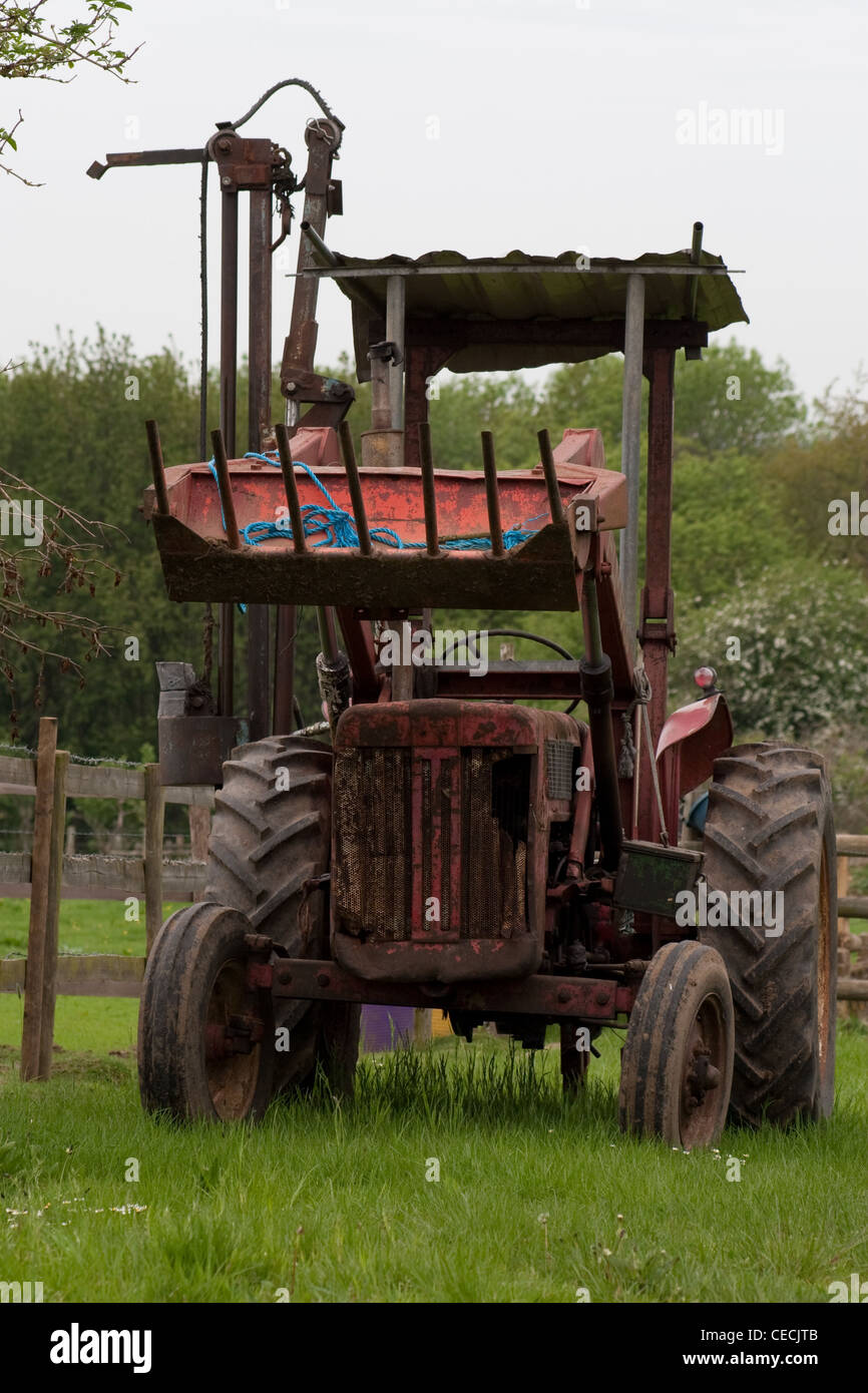 An old red tractor sitting in a field with worn tyres and its hay scoop ...