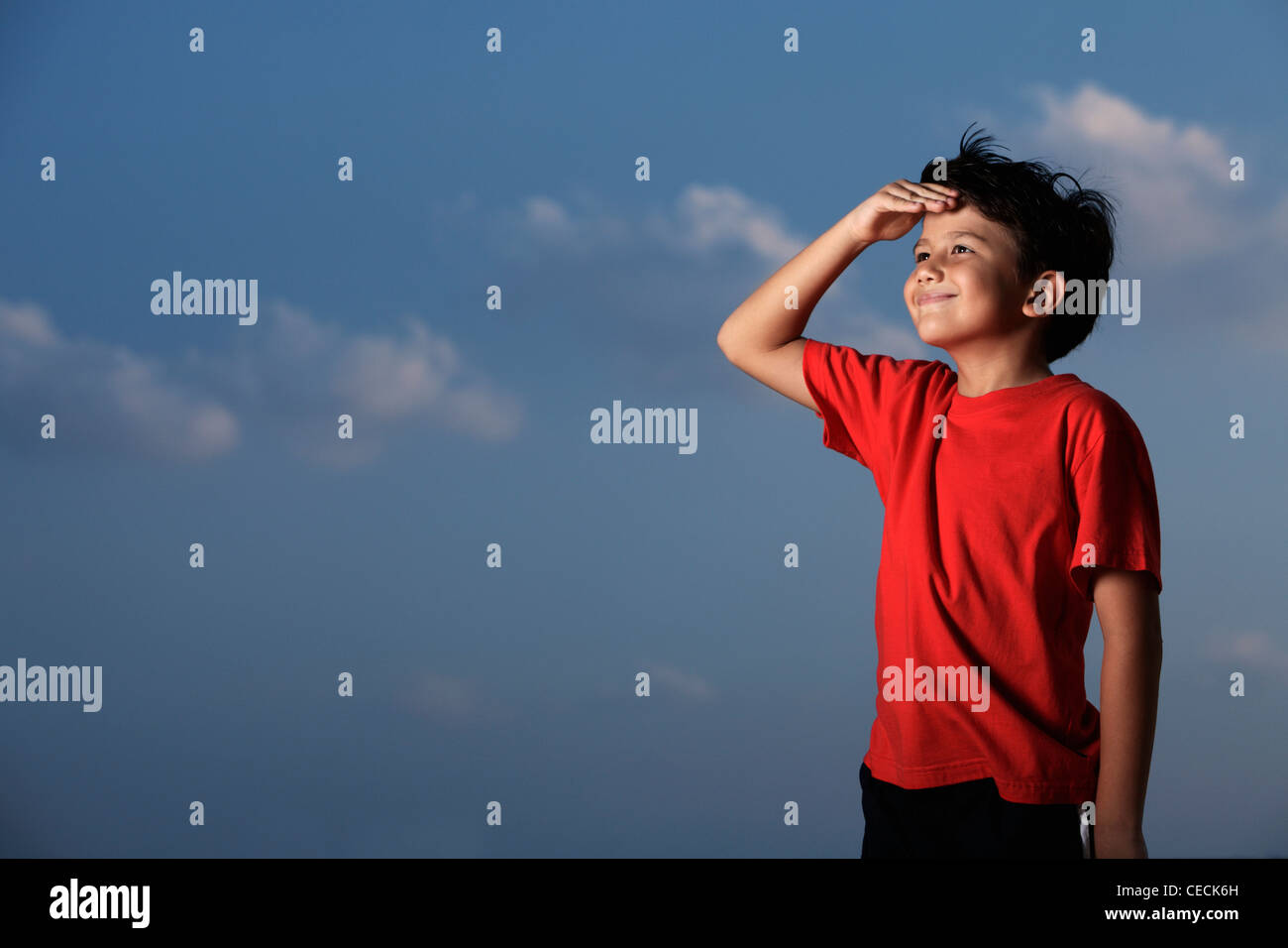 Young boy wearing a red shirt looking out with hand shielding eyes ...
