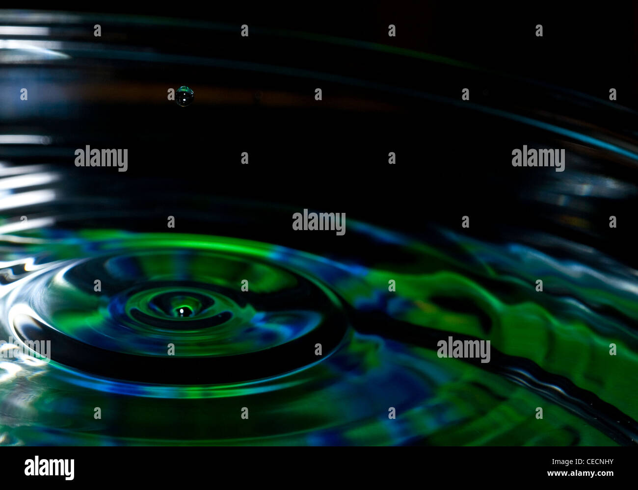 Drop of water falling into a pool with ripples and blue and green ...