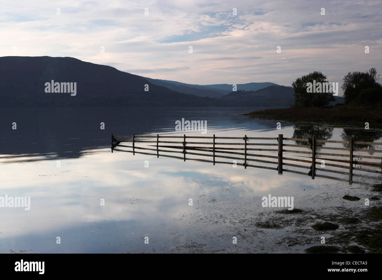 Dusk over a calm lake. A fence is reflected in the water as it is ...