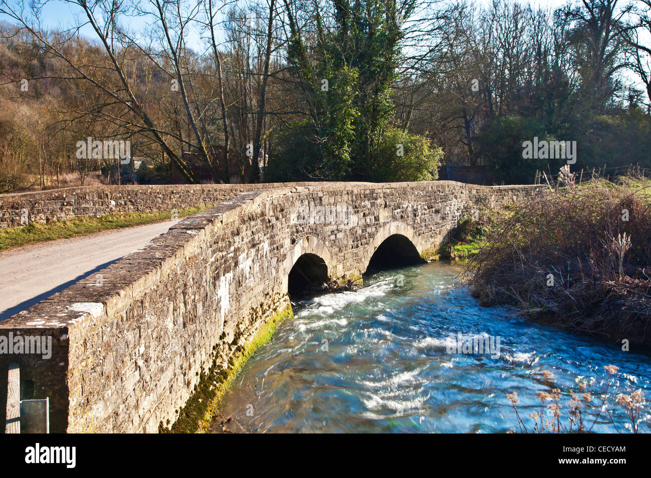 An arched Cotswoldstone bridge over a small river the By Brook in the ...