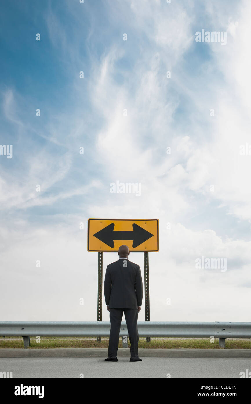 African American businessman looking at conflicting road sign Stock ...