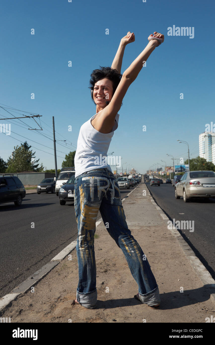girl with lifted hands stands in half-turn on middle of road among cars ...