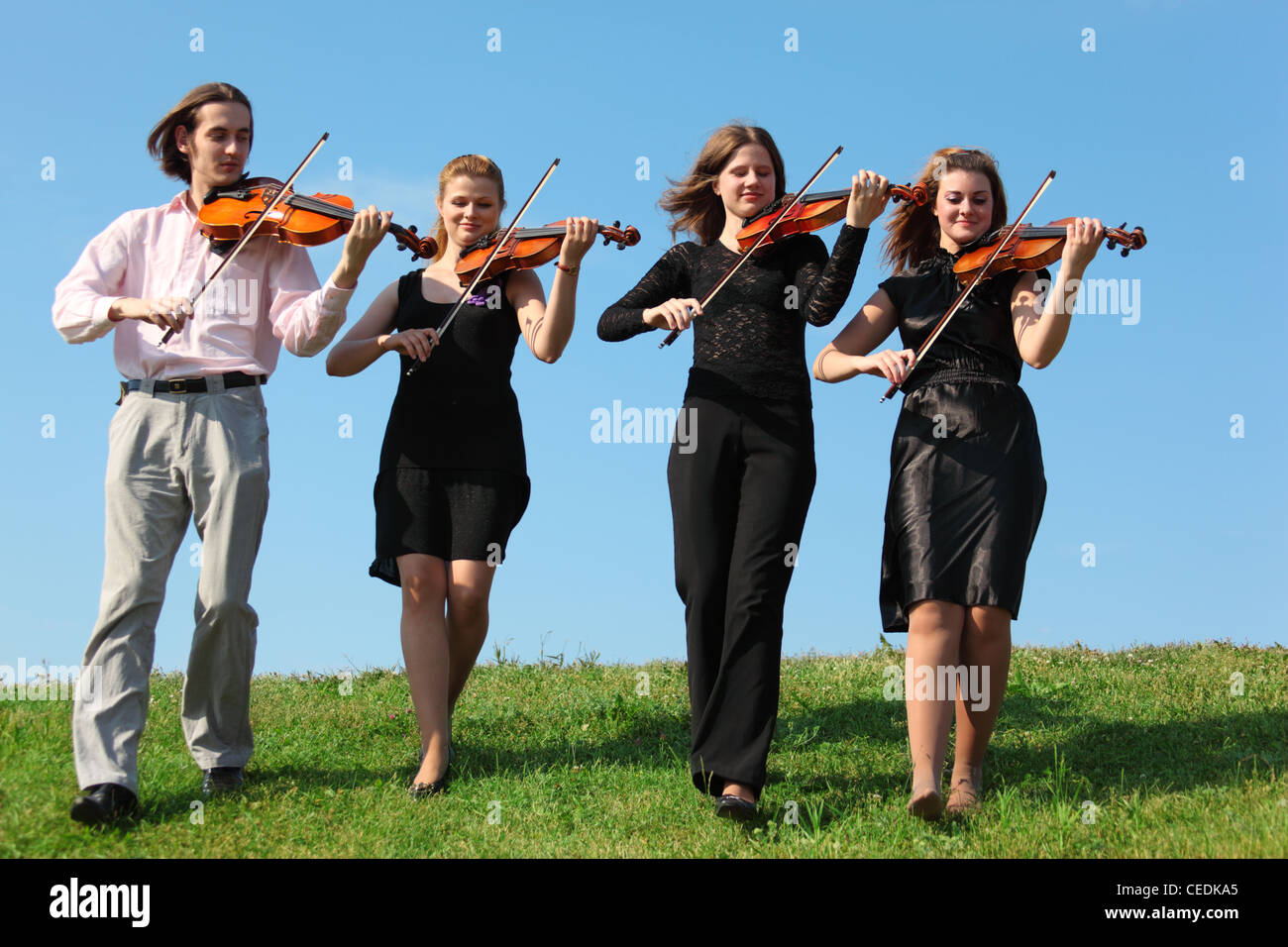 Four musicians go and playing violins against sky, front view Stock ...