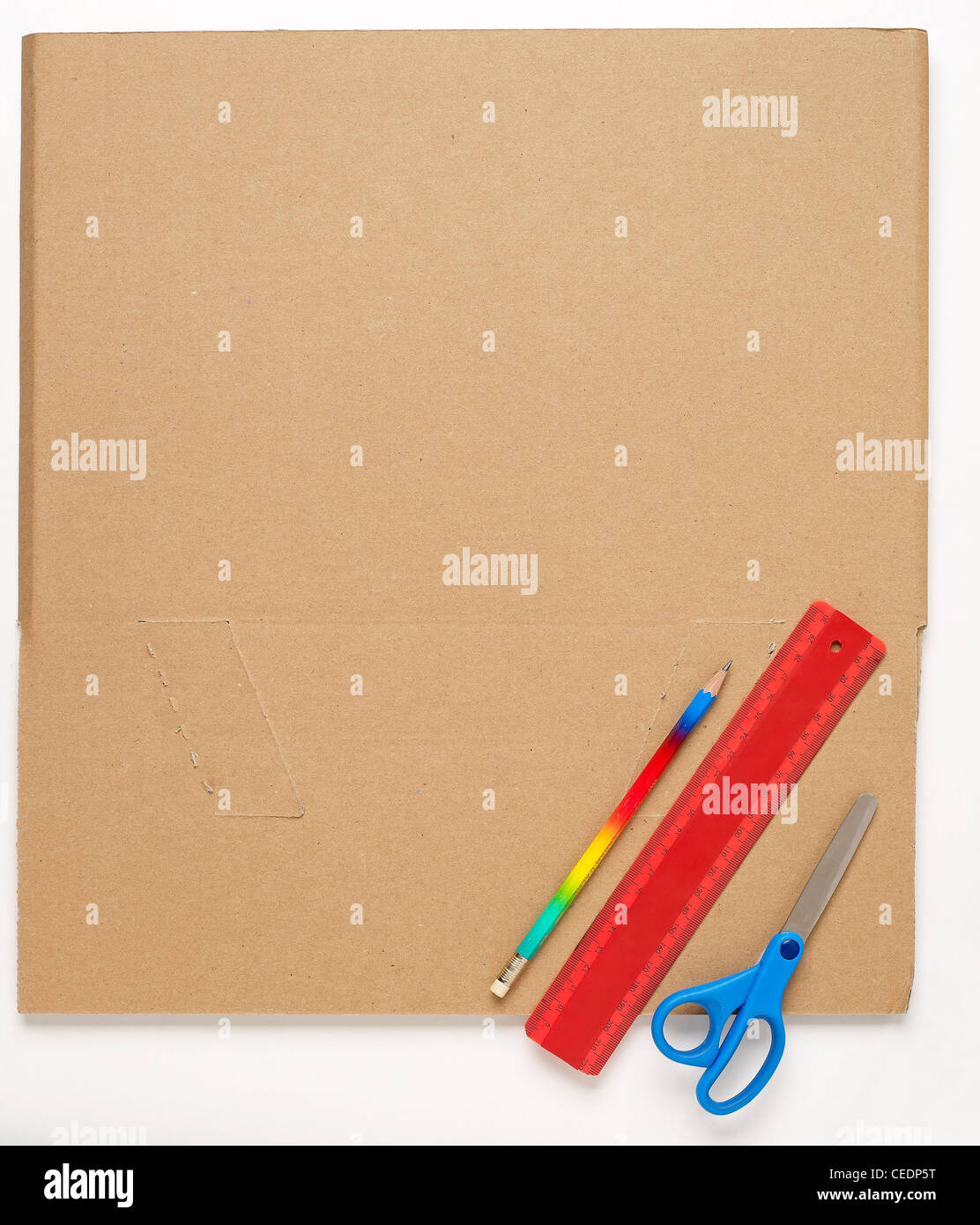 Red ruler, rainbow-coloured pencil, and pair of scissors, on piece of ...