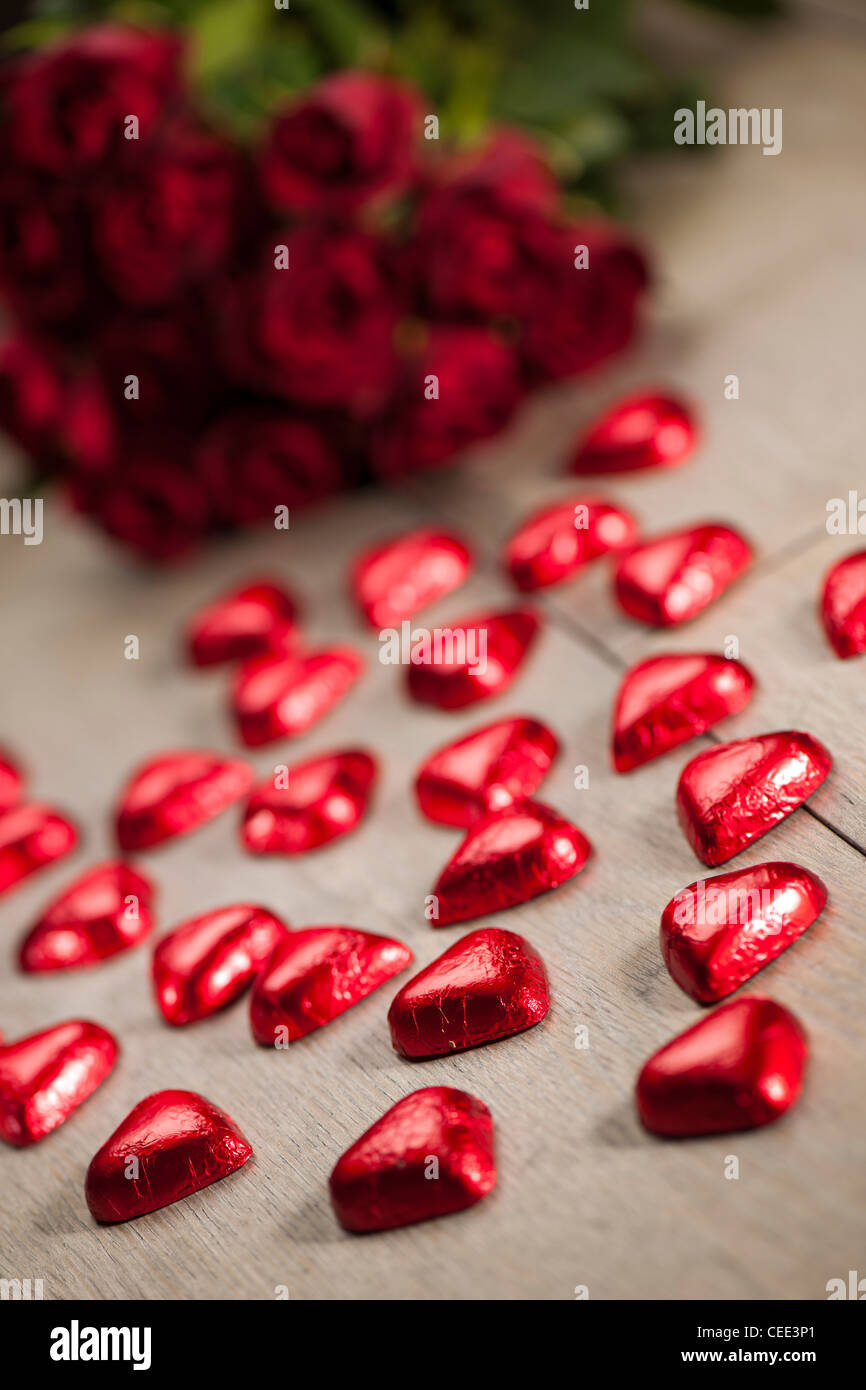 Chocolate shaped heart sweets wrapped in red foil and red roses Stock ...