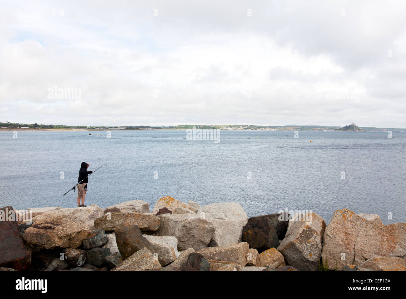 Lone fisherman with rod and reel fishing off rocks at Penzance ...