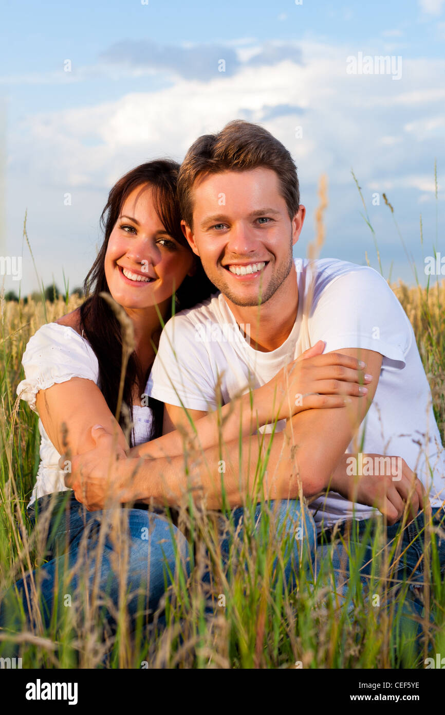 Happy couple sitting on a meadow or grainfield in summer embracing each ...