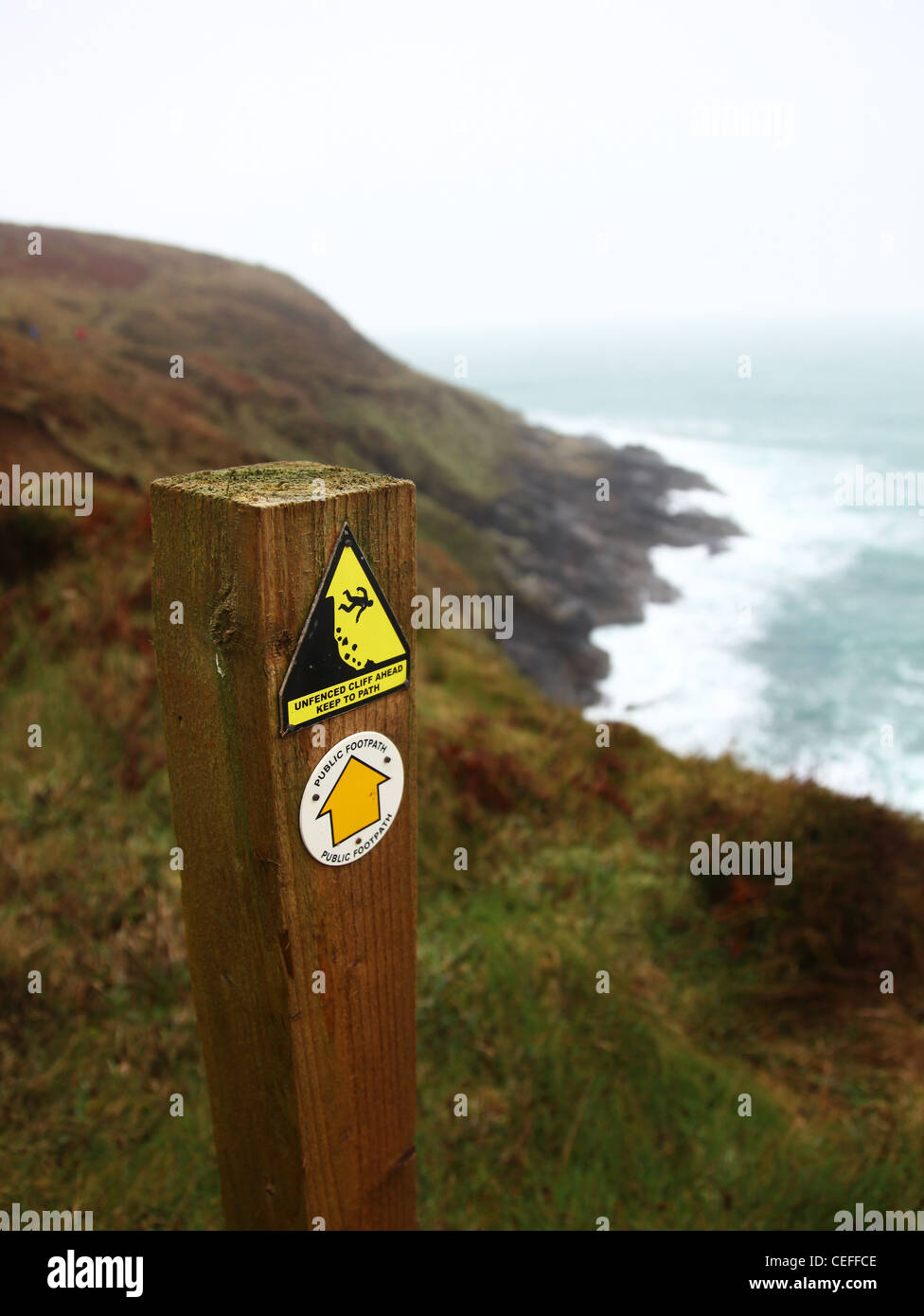 A sign post warning of an unfenced path next to the cliff edge on a ...