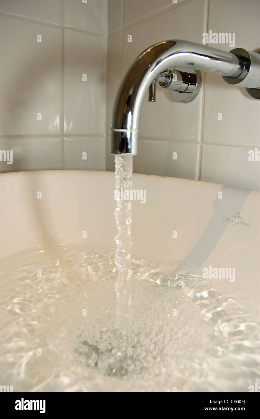 Close up of water pouring from chrome tap into circular white ceramic ...