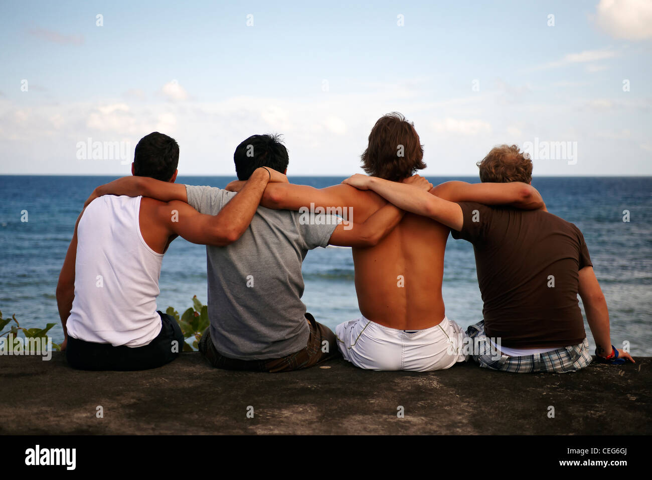 four friends with arms around each other looking out over the Caribbean ...