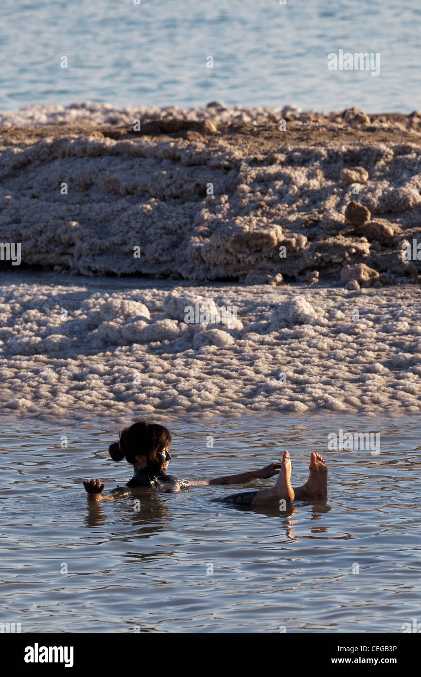 A woman floating in the Dead Sea, her face covered in mud with salt ...