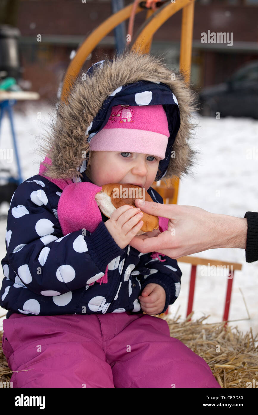 Adorable toddler in winter clothing eating a roll Stock Photo - Alamy