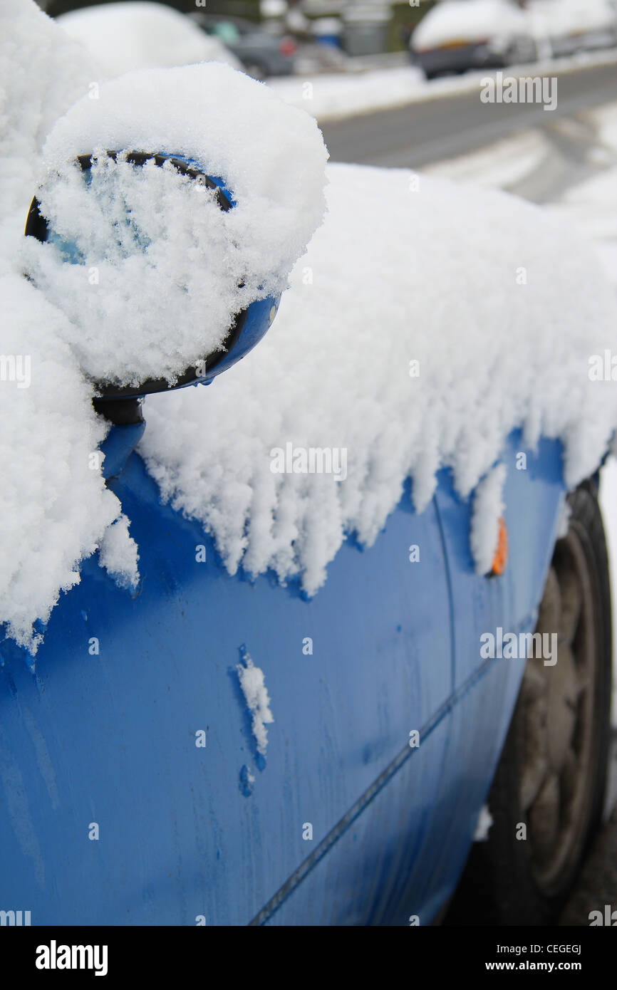 blue car covered in snow. Detail of side mirror and side of the front ...