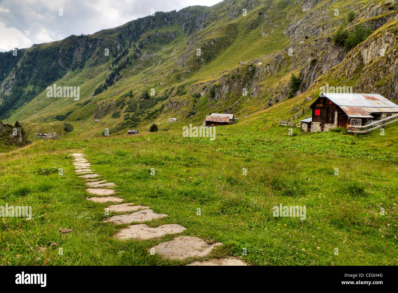 hiking path leading along alpine valley with wooden huts, Switzerland ...