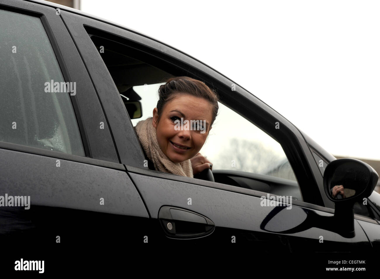 Female in her 20s driving car looking behind out of driver side window ...